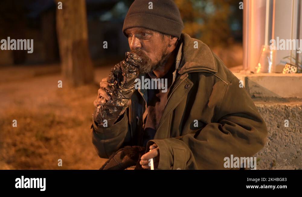 Homeless sick man drinking vodka sitting on the street at night Stock ...