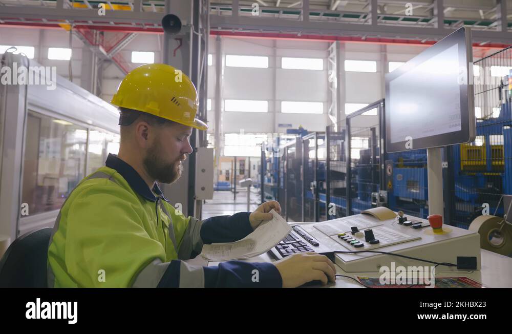 Factory worker in uniform and hard hat looks to blueprints for ...