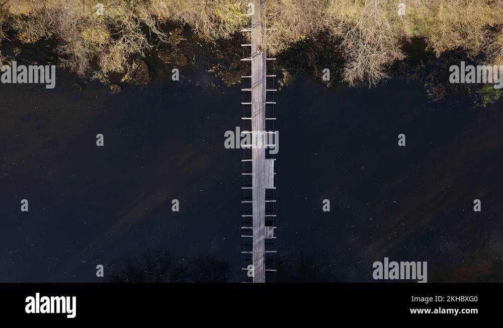 Aerial top down man walking along wooden suspension bridge over river ...