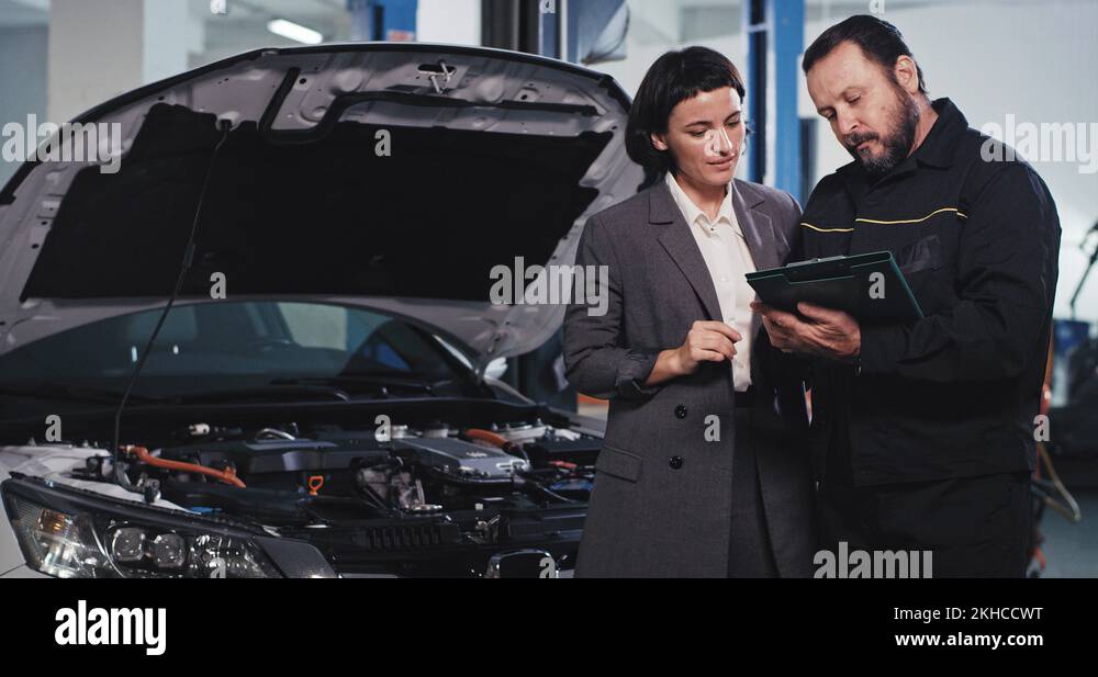 In the large modern garage mechanic man in a uniform with a map have a ...