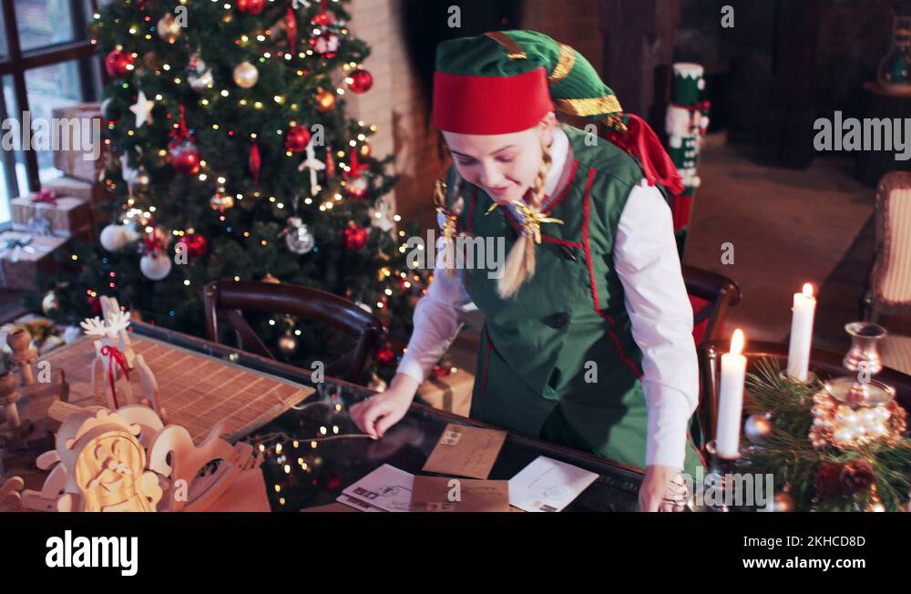 Merry elf girl in a green suit transfers letters on a table in a room ...