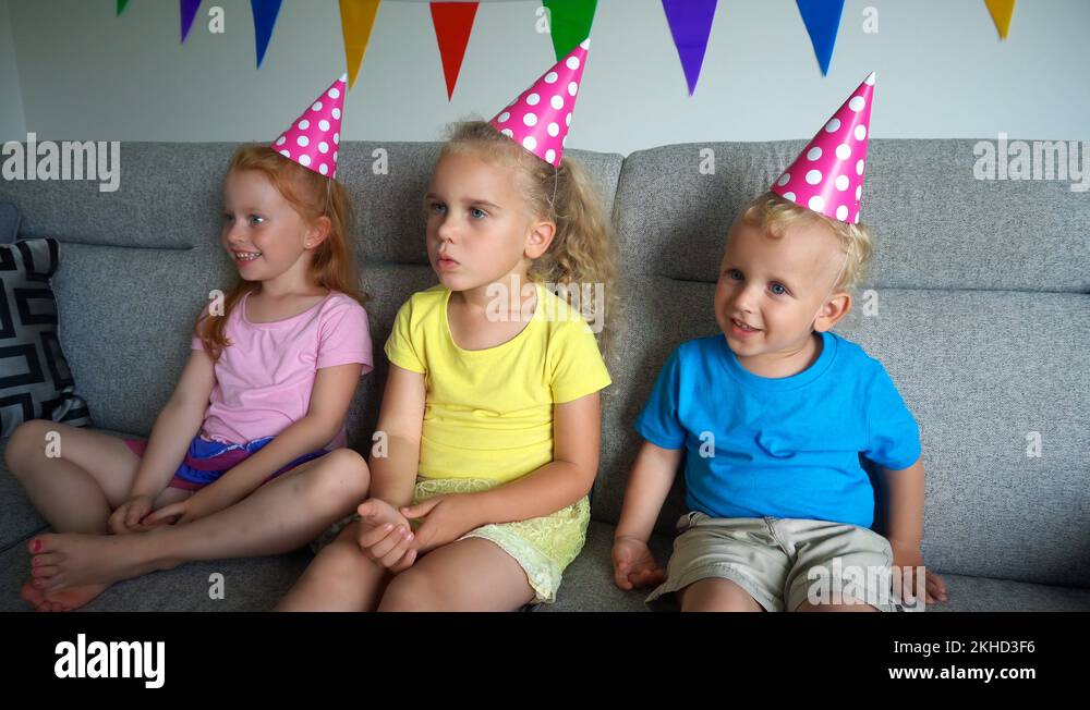 Laughing kids with party hats watch tv. Little boy and two girls ...