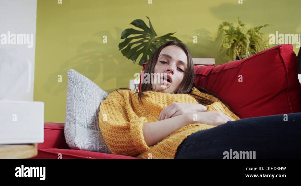 Poor unhealthy young woman lying on couch at home blowing her nose in ...