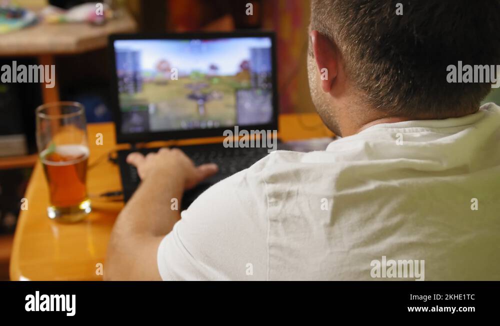 Man plays computer games on a computer and drinks beer from the glass ...