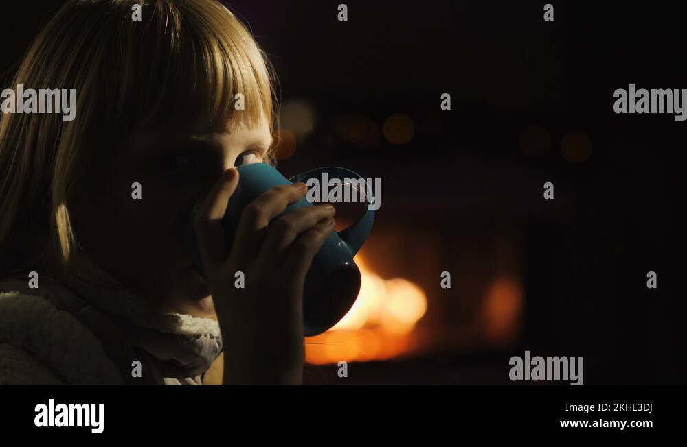 Girl drinks tea sitting by the window, a fireplace and a Christmas tree ...