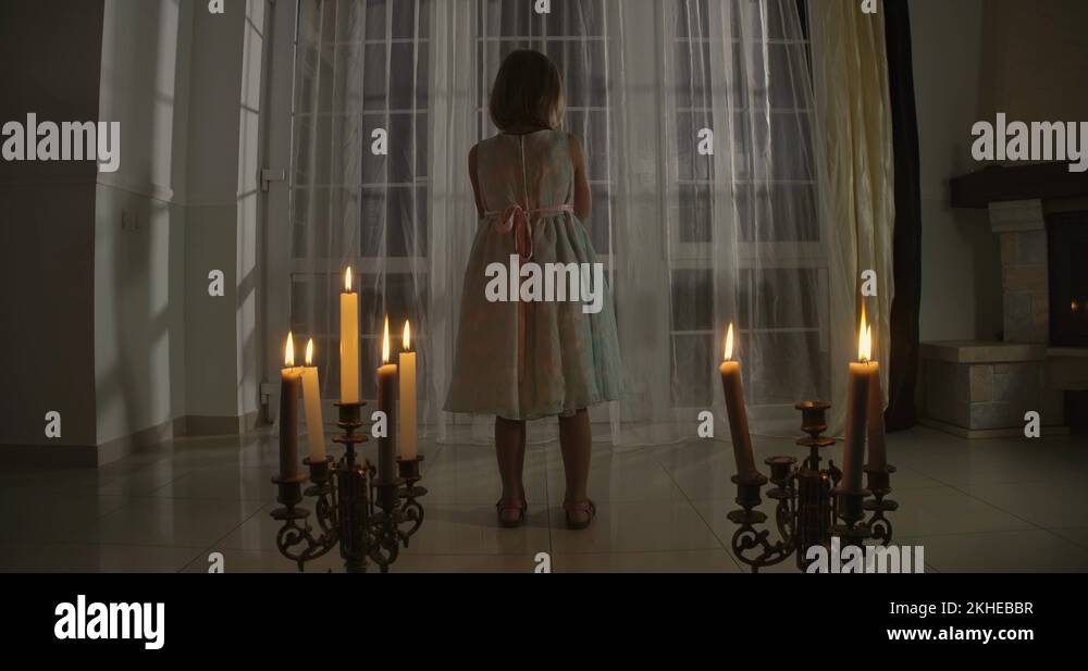 Back view of strange Caucasian girl standing in candlelight. Weird ...