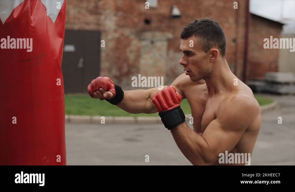 Close side view of muscular male boxer practicing punches and kicks ...