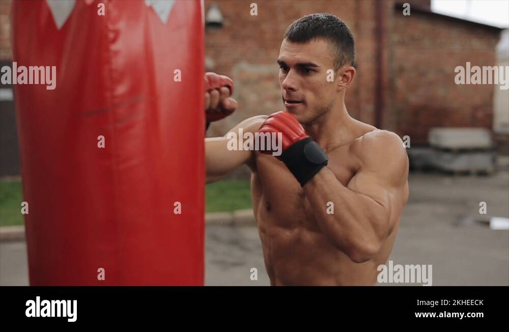Close side view of muscular male boxer practicing punches and kicks ...