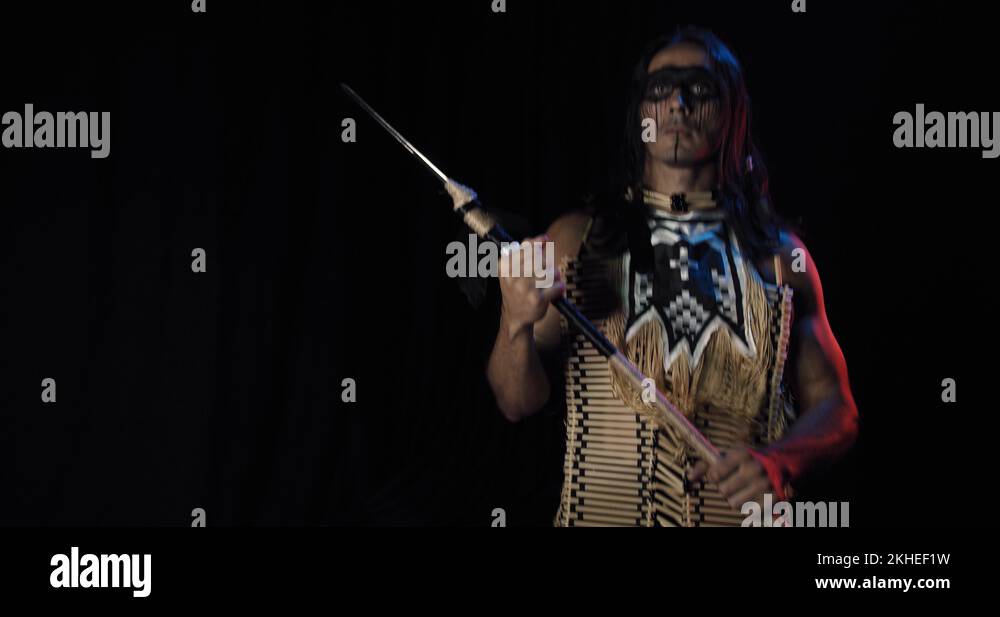 Cherokee man wearing traditional costume is jumping and holding a spear ...