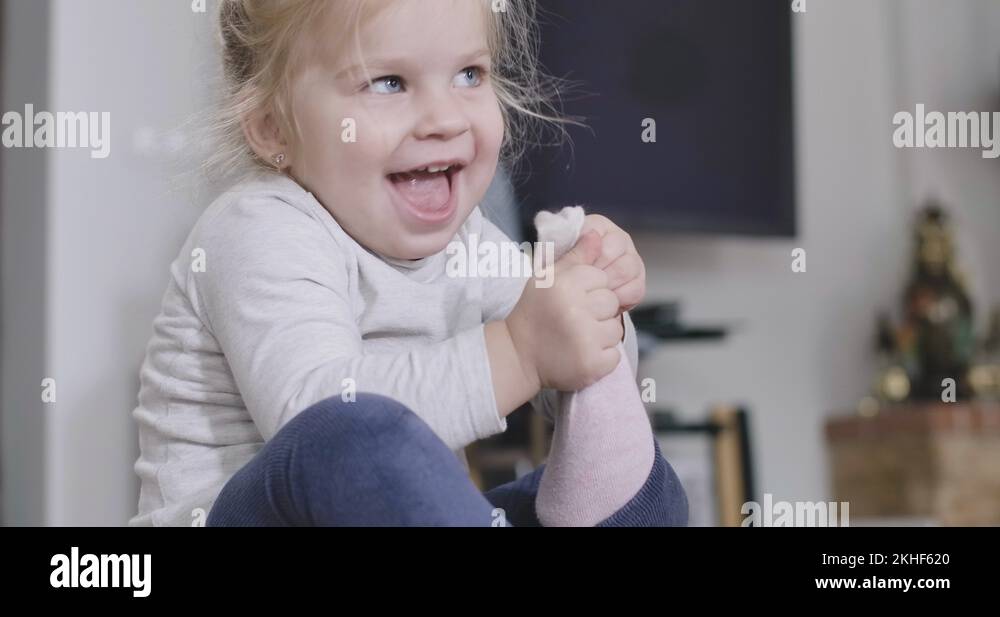 Close-up portrait of positive little girl taking off pink sock. Blond ...