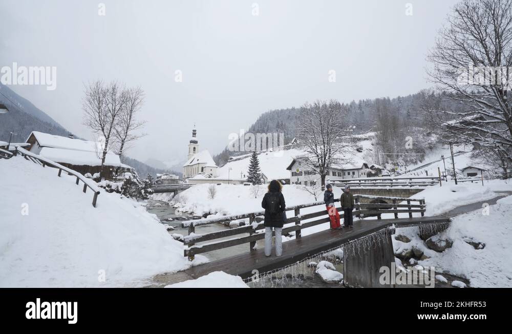 Snow falling on family on small bridge looks up at church in Bavarian ...