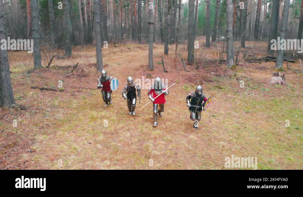 Four men knightes running in the row in the forest in full armour - day ...