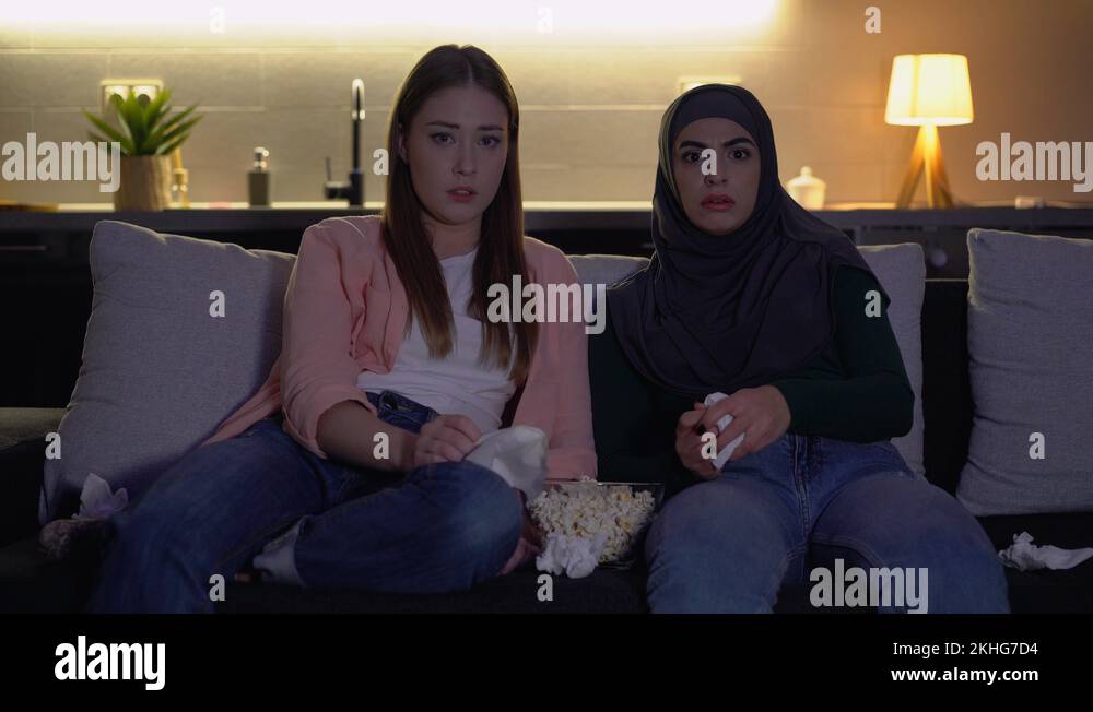 Two girls watching sad film on couch, crying and wiping tears, leisure ...