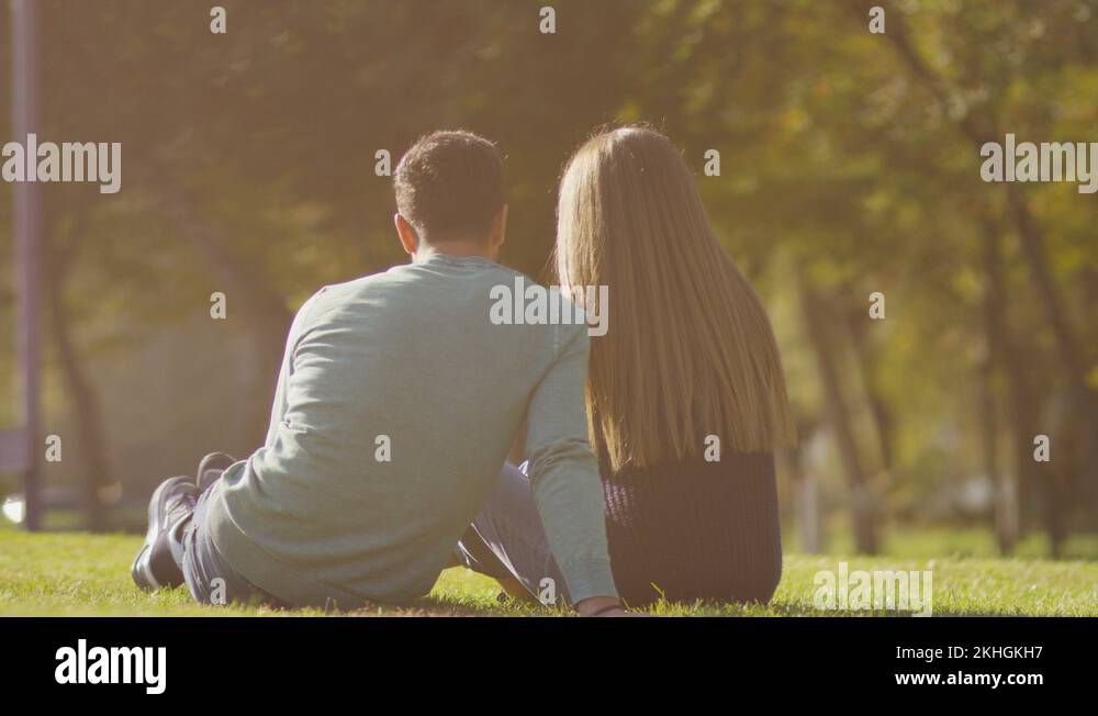 Back view of lovely romantic couple sitting on lawn and hugging each ...