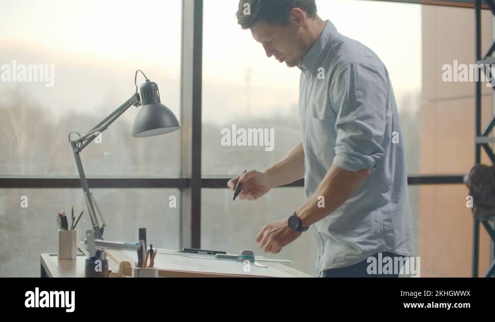 Architect man sits at drafting table in modern industrial office during ...