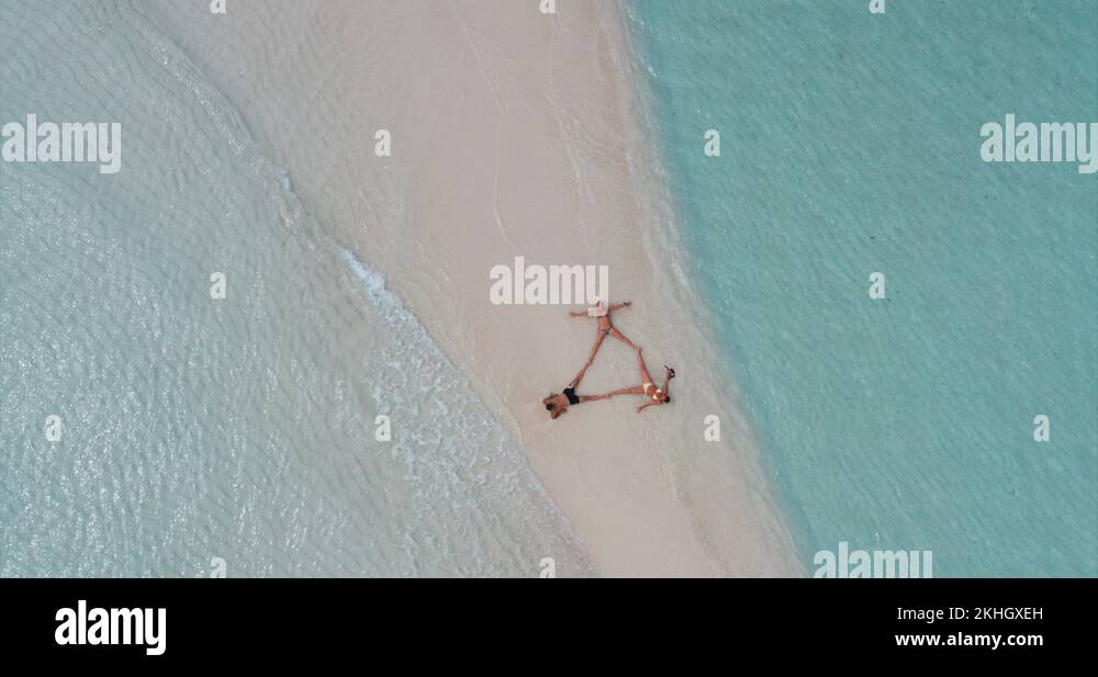A group of friends lying in the water in a triangle form on the beach ...