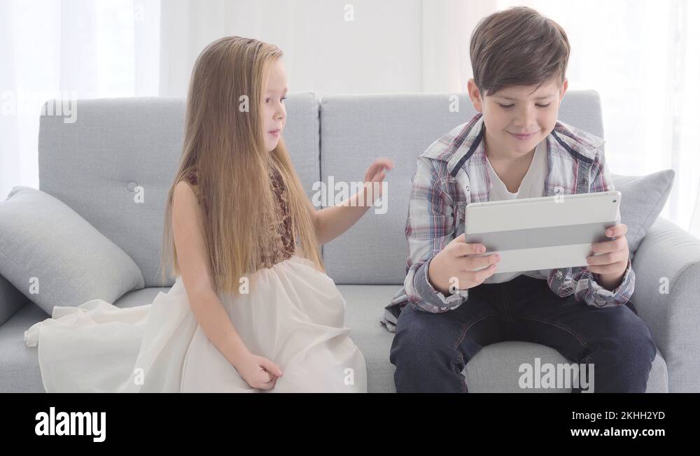 Two Caucasian children sitting on couch. Cute Caucasian girl touching ...