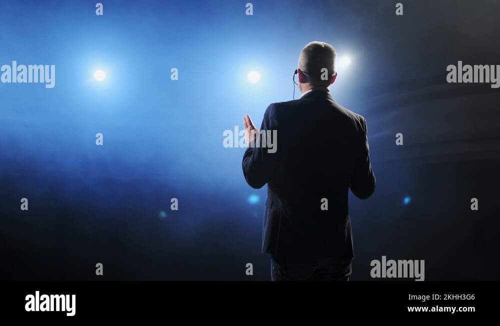 Rear view of men speaking through a microphone in dark conference hall ...