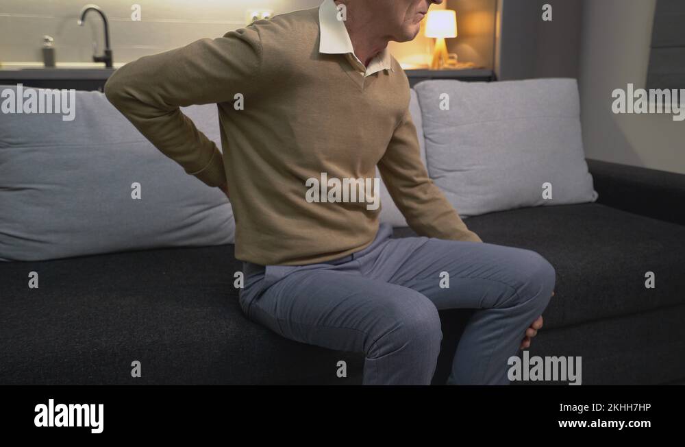 Elderly male feeling back pain, sitting on sofa, spinal disk disease ...