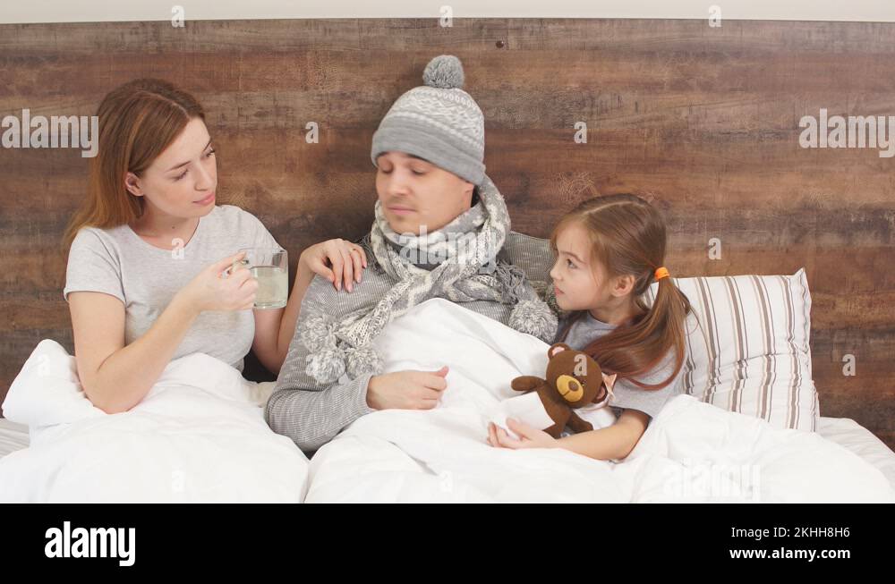 Sick man with high temperature lying on bed with careful child and wife ...