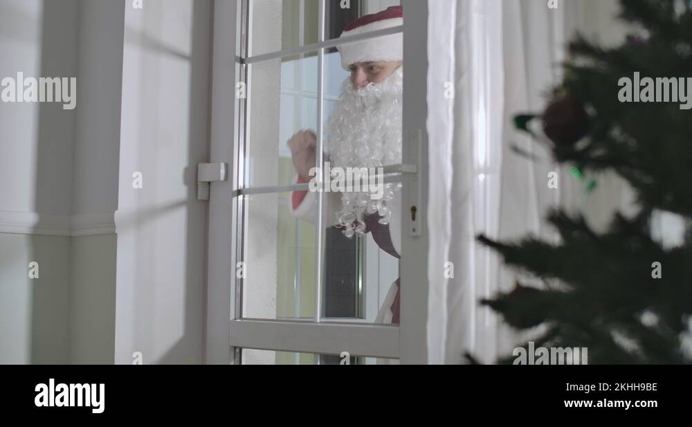 Santa Claus standing behind glass entrance door and waving as cute ...