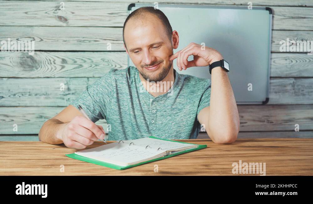 Pensive bearded guy writing in notepad ideas, dreaming smiling male ...