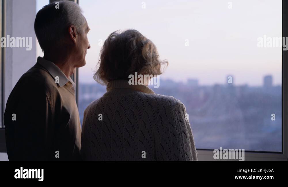 Elderly married couple standing by window together, caring husband ...
