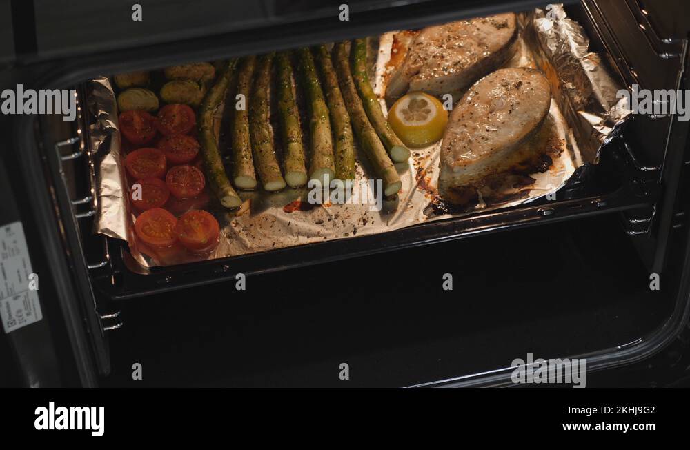 Woman getting prepared dinner out of oven. Cooked fish and vegetables ...