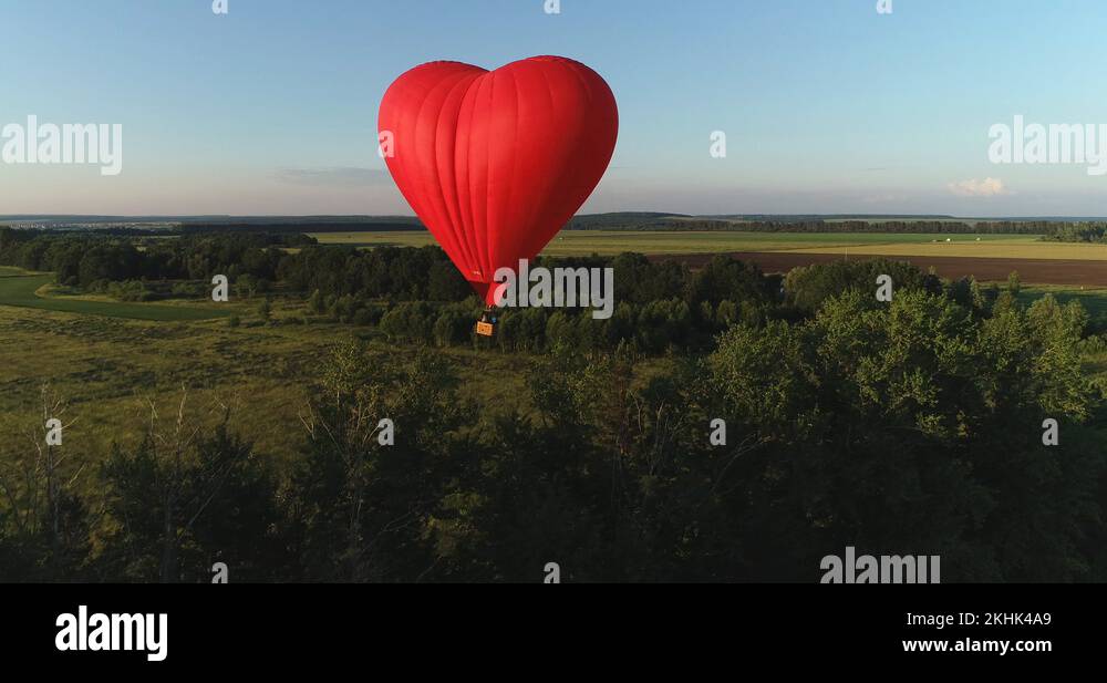 Hot air balloon shaped heart flight above field and forest Stock Video ...