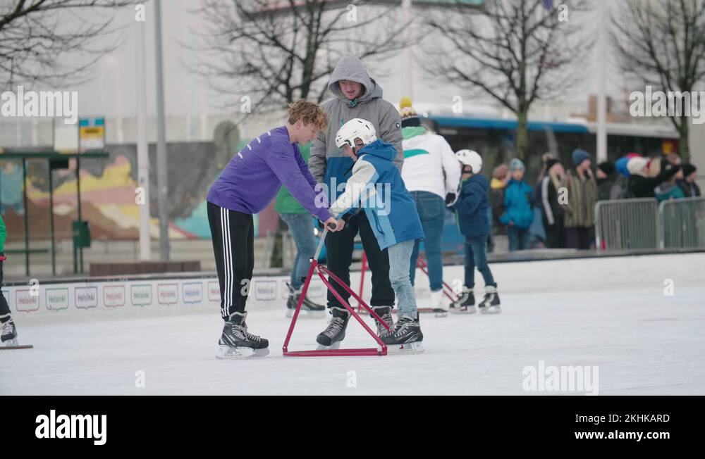 Father and two sons skating using a tube-stand on ice rink in Finland ...