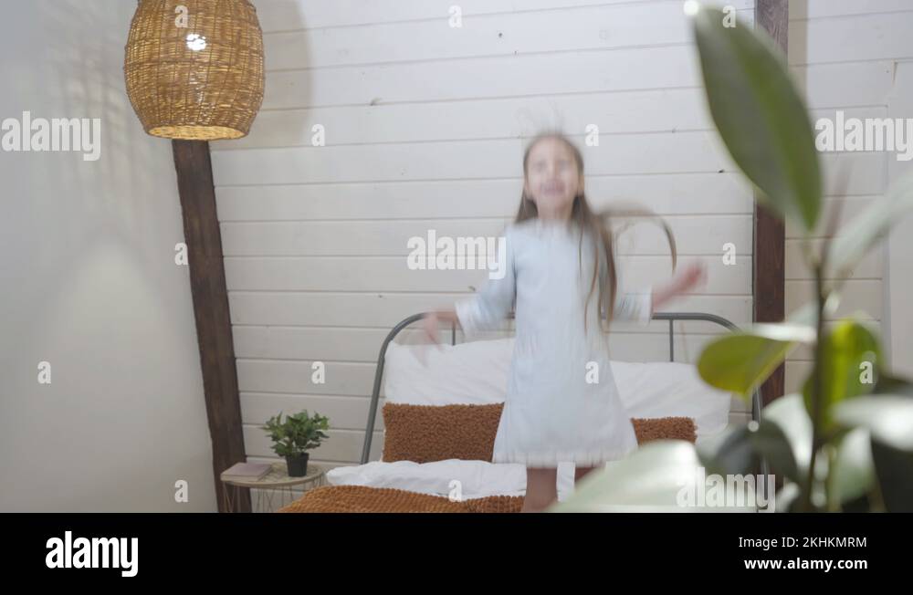 Cheerful little girl jumping on bed and falling down. Cute brunette ...