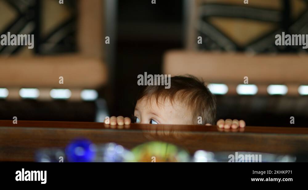 Adorable baby appearing from under table. Cute infant peeking out head ...