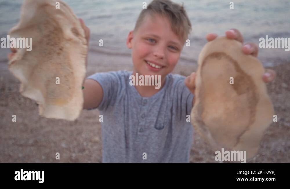 Boy playing at seashore of Egypt holding coral reefs big seashells in ...