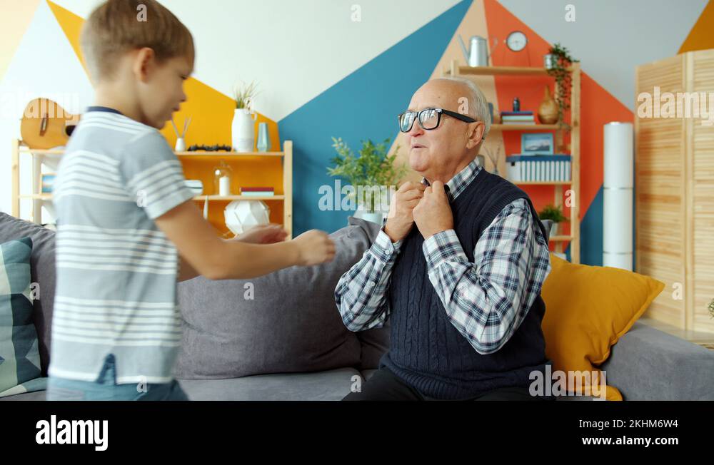 Caring little boy helping old man with clothing then having fun indoors ...