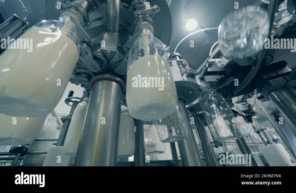 Factory mechanism is filling transparent bottles with fresh milk ...