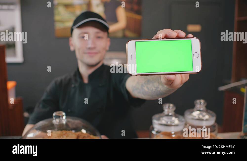 Cafe waiter holding green screen tablet to customer at bar counter with ...