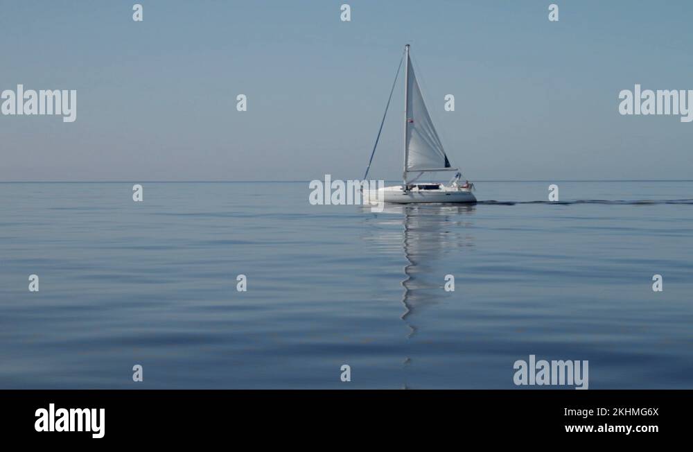 sailboat with reflection motor sailing across calm still blue water in ...