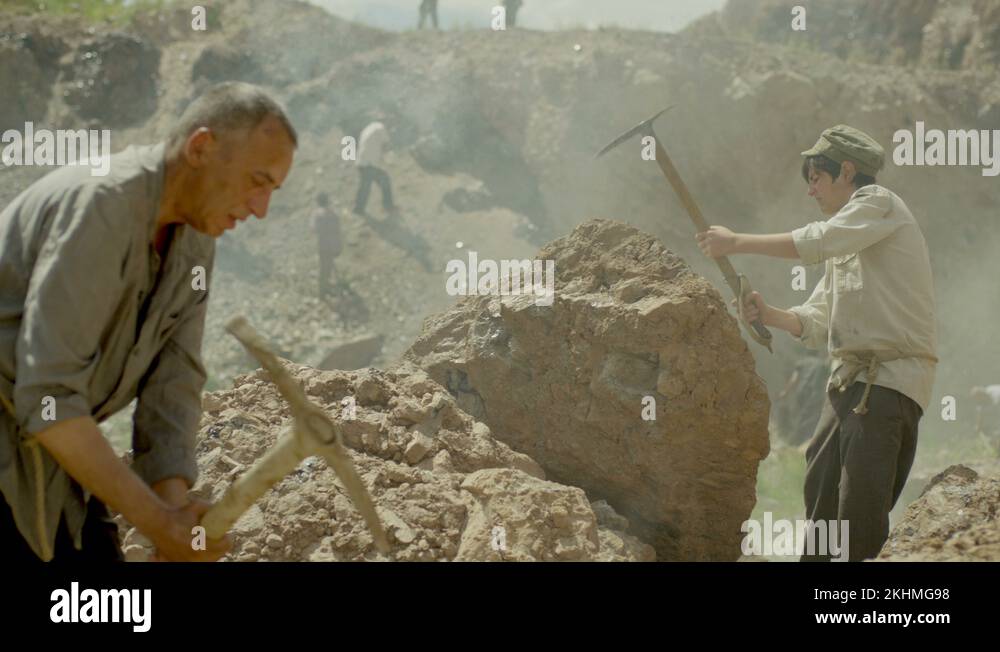 Young miner boy is working in a quarry . Many workers are mining with ...