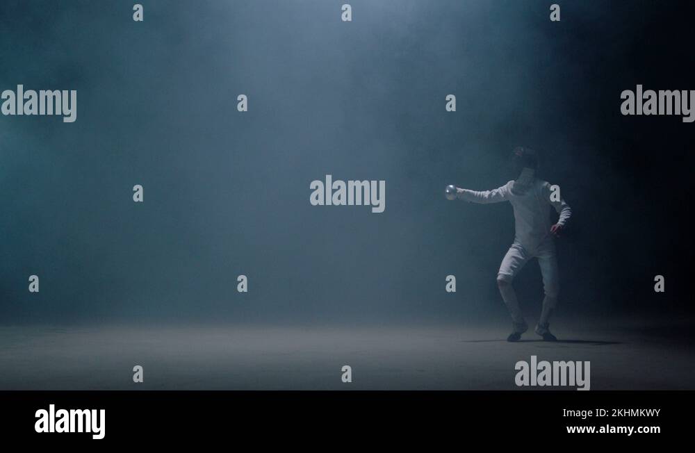 Professional fencer in uniform practicing maneuvers with sword in dark ...