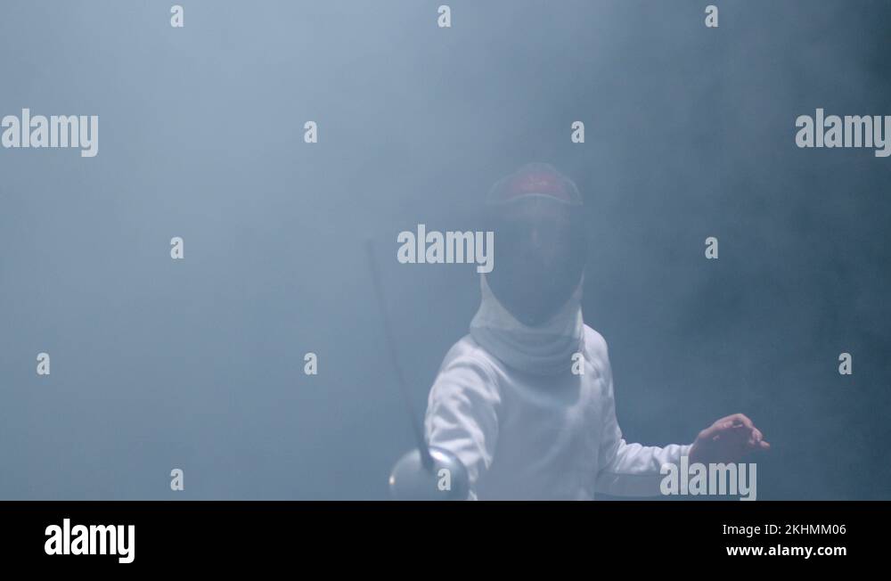 Professional fencer in uniform practicing maneuvers with sword in dark ...