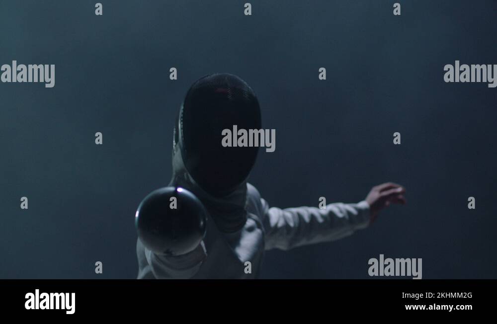 Professional fencer in uniform practicing maneuvers with sword in dark ...