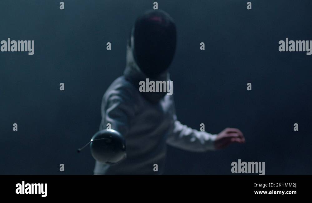 Professional fencer in uniform practicing maneuvers with sword in dark ...