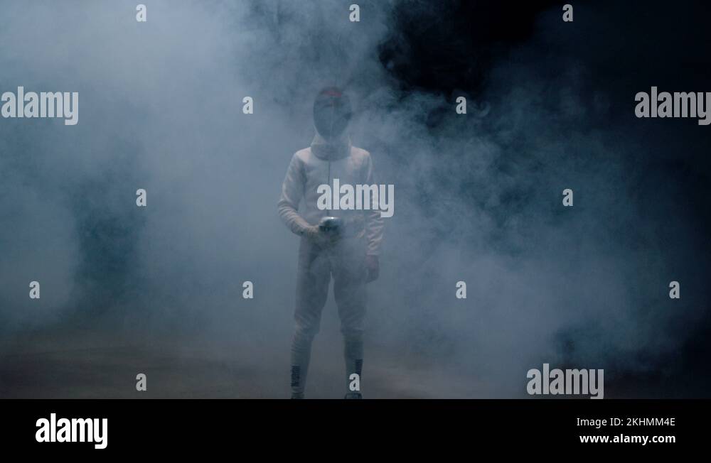 Professional fencer in uniform practicing maneuvers with sword in dark ...
