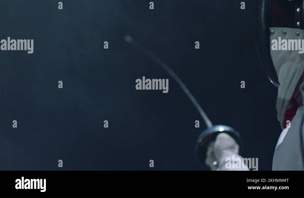 Professional fencer in uniform practicing maneuvers with sword in dark ...