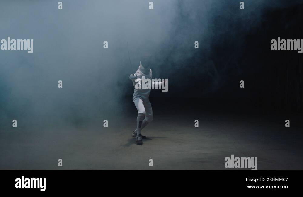 Professional fencer in uniform practicing maneuvers with sword in dark ...