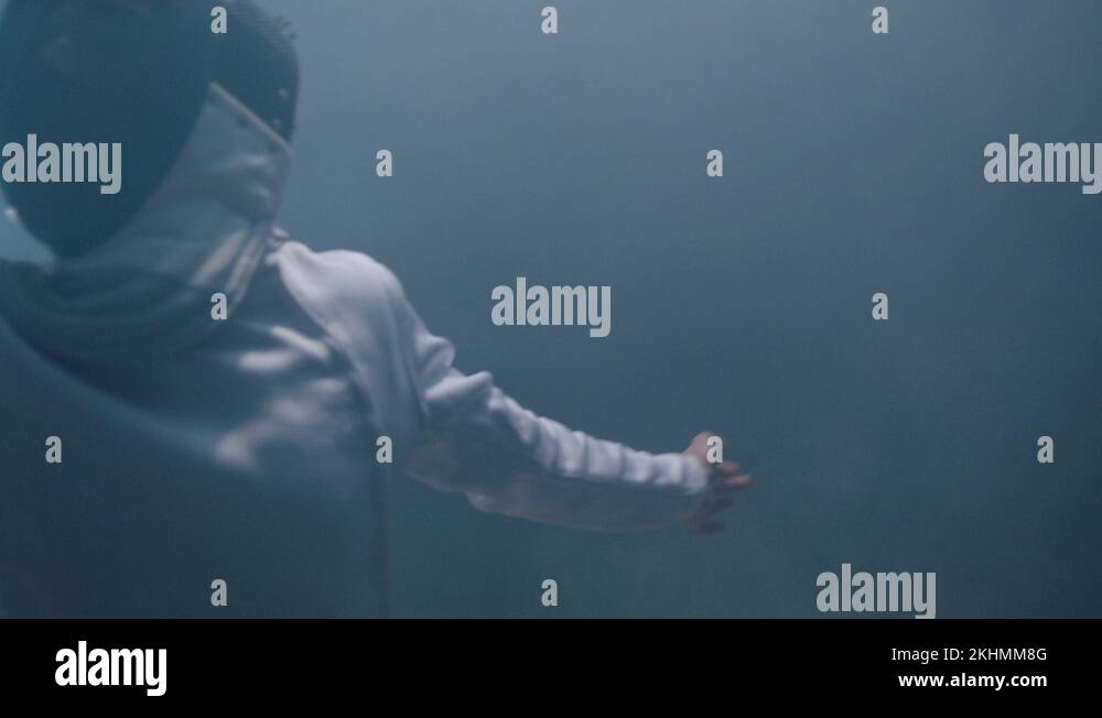 Professional fencer in uniform practicing maneuvers with sword in dark ...