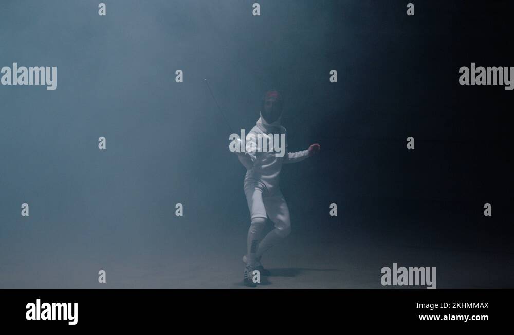 Professional fencer in uniform practicing maneuvers with sword in dark ...