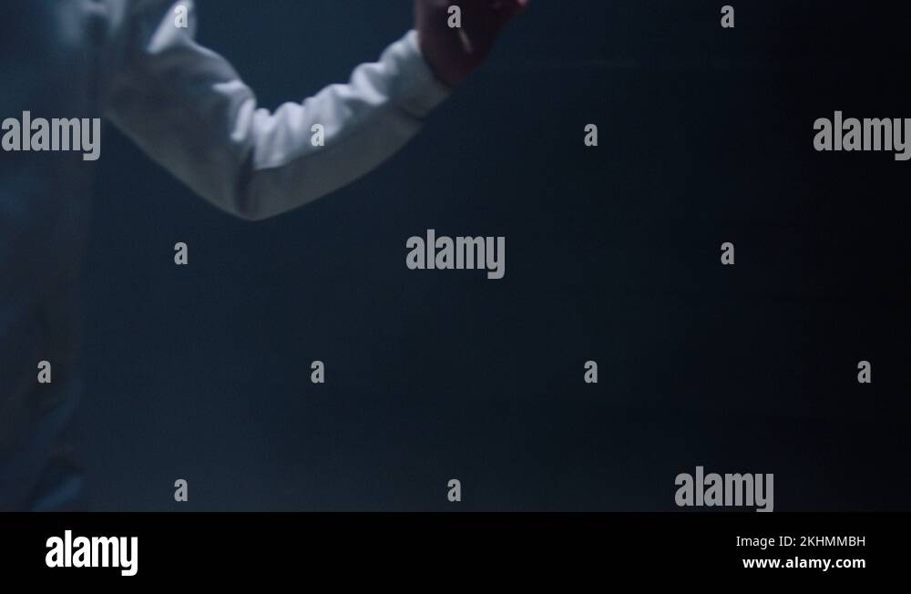 Professional fencer in uniform practicing maneuvers with sword in dark ...