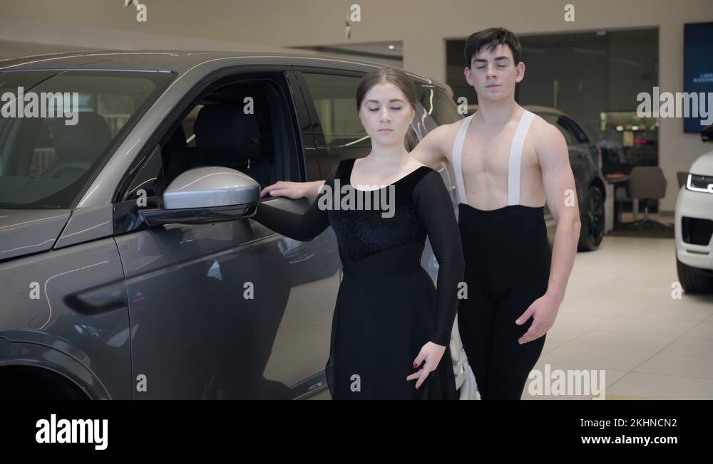 Two young Caucasian ballet dancers standing next to car in dealership ...