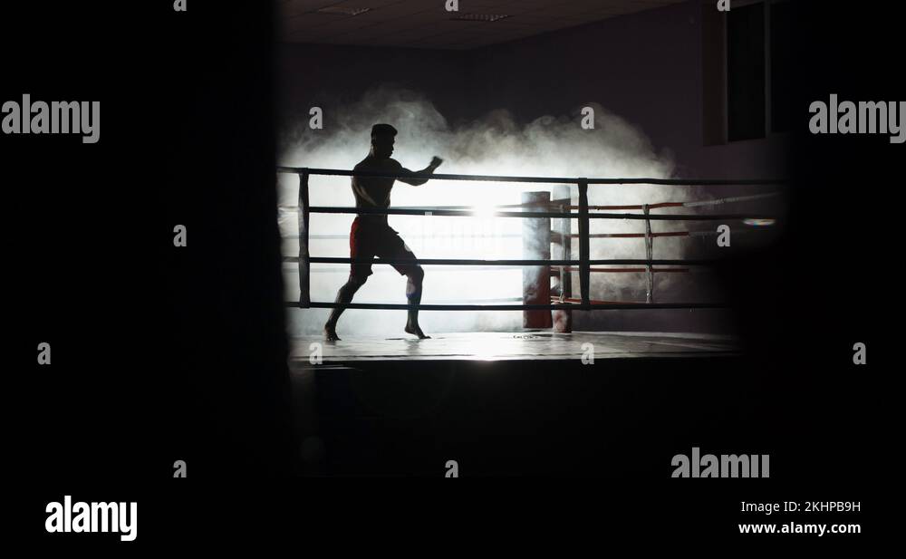 Dedicated athlete doing a shadow fight on boxing ring, practicing muay ...